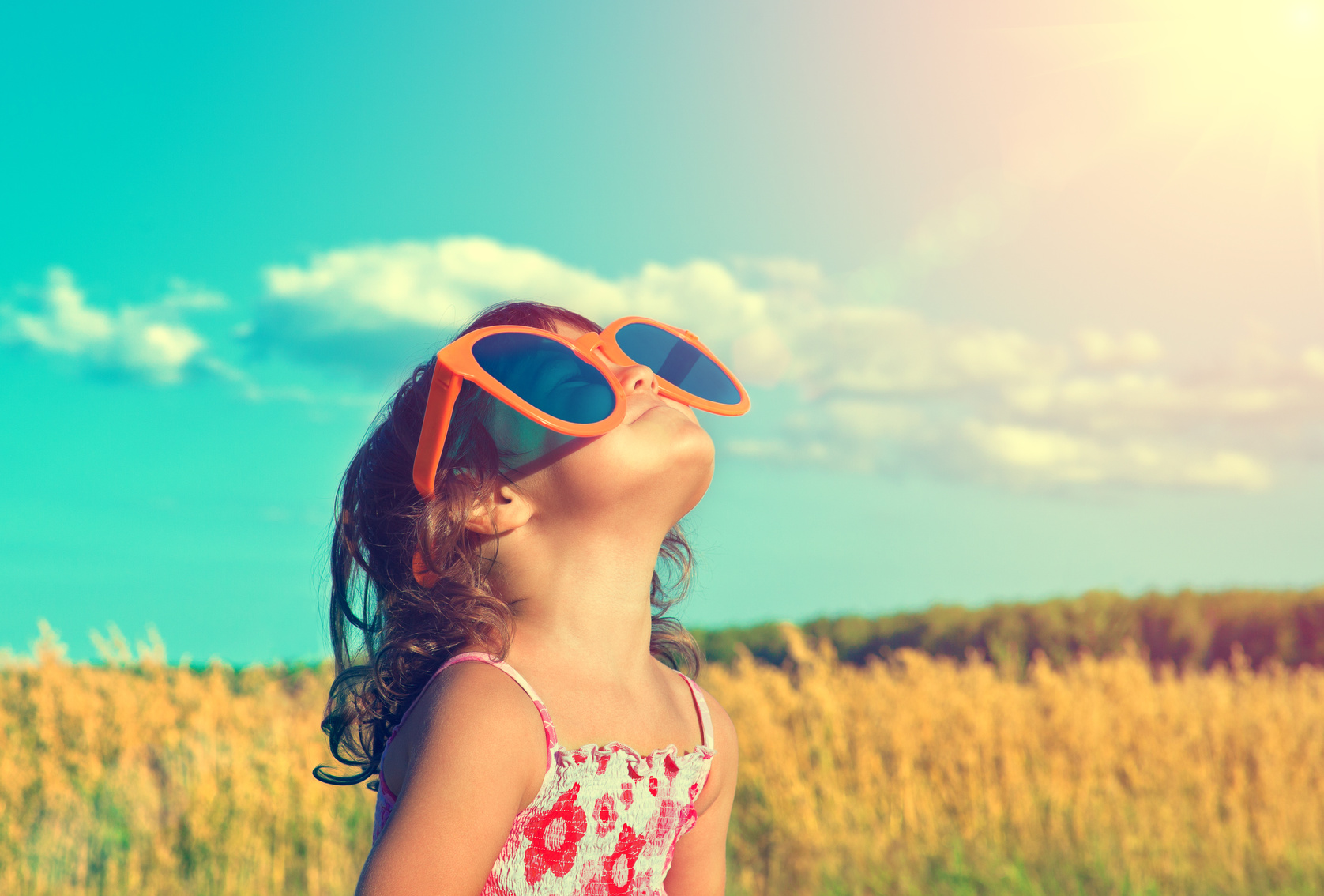 Happy little girl with big sunglasses looking at the sun